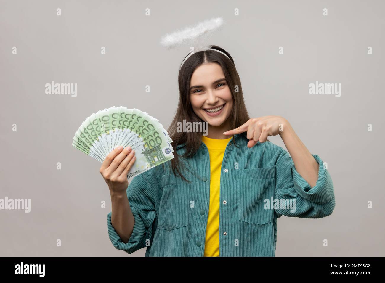 Cheerful dark haired woman with halo on head pointing finger on bunch ...