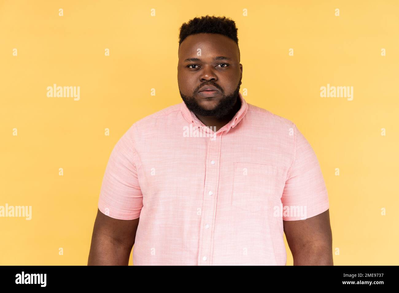 Portrait of serious strict young adult man wearing pink shirt standing ...