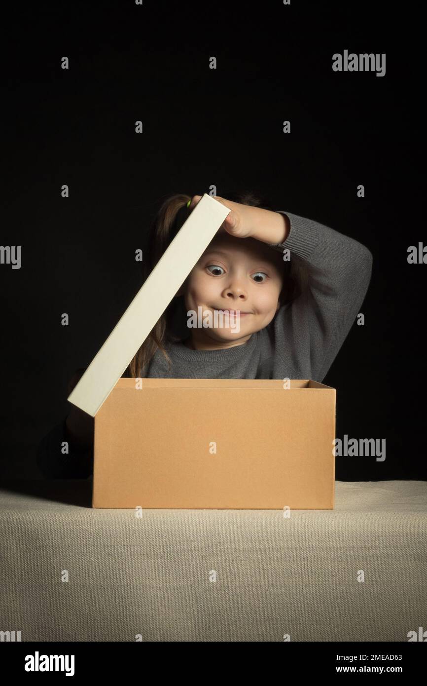 Emotional happy and surprised little girl opens a long-awaited package ...