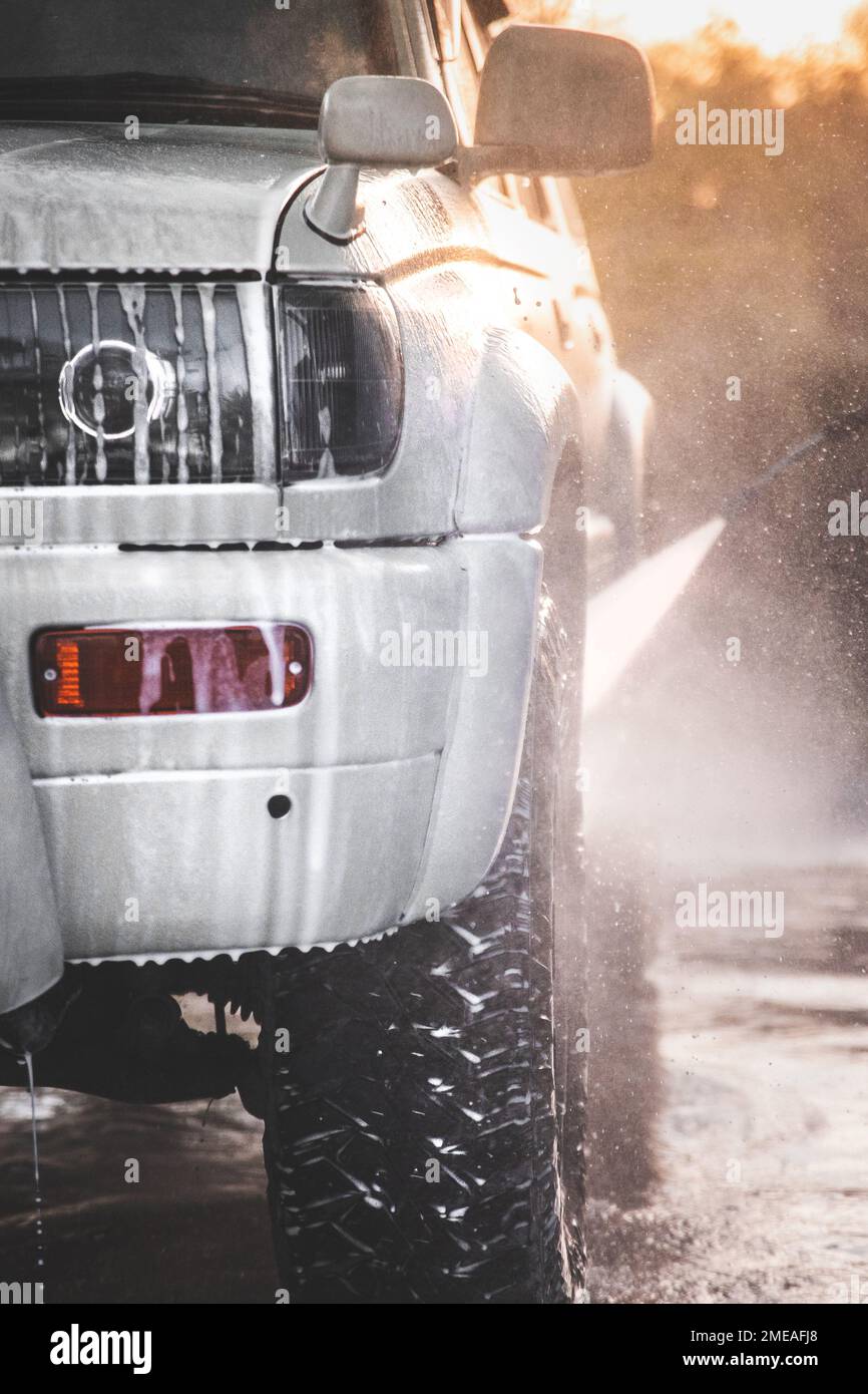 Washing white car at a self-service car wash with a high-pressure water ...