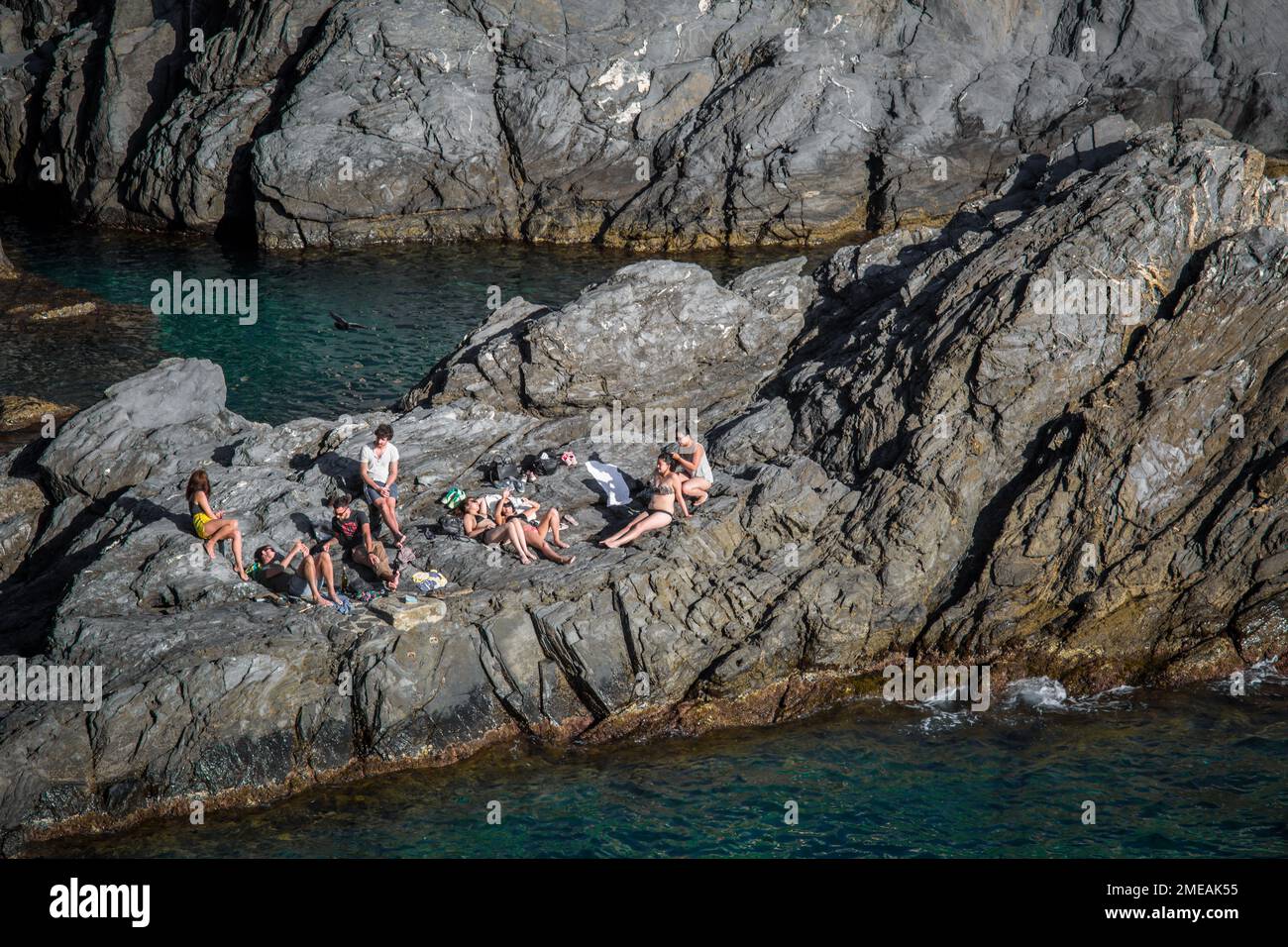 Group of young adults sun bathing on rocks in Manarola, Cinque Terre ...