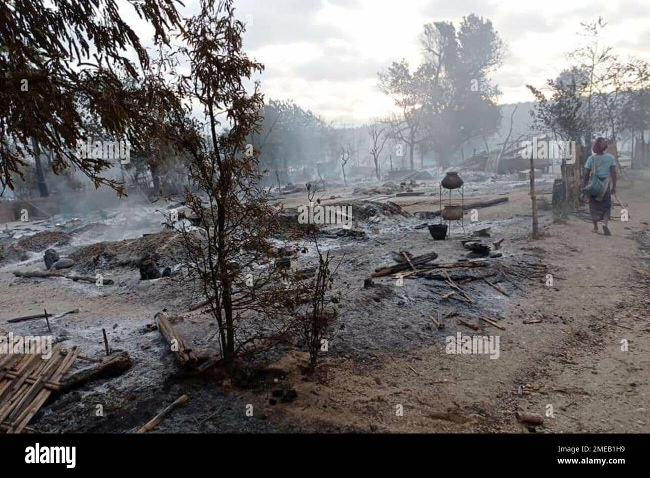 A resident walks past smoldering houses in the Kinma village, Pauk ...