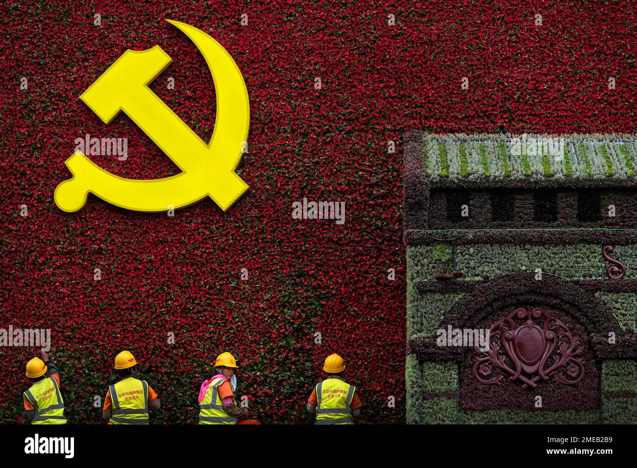 Workers install flowers on a decoration with a Communist Party's logo ...