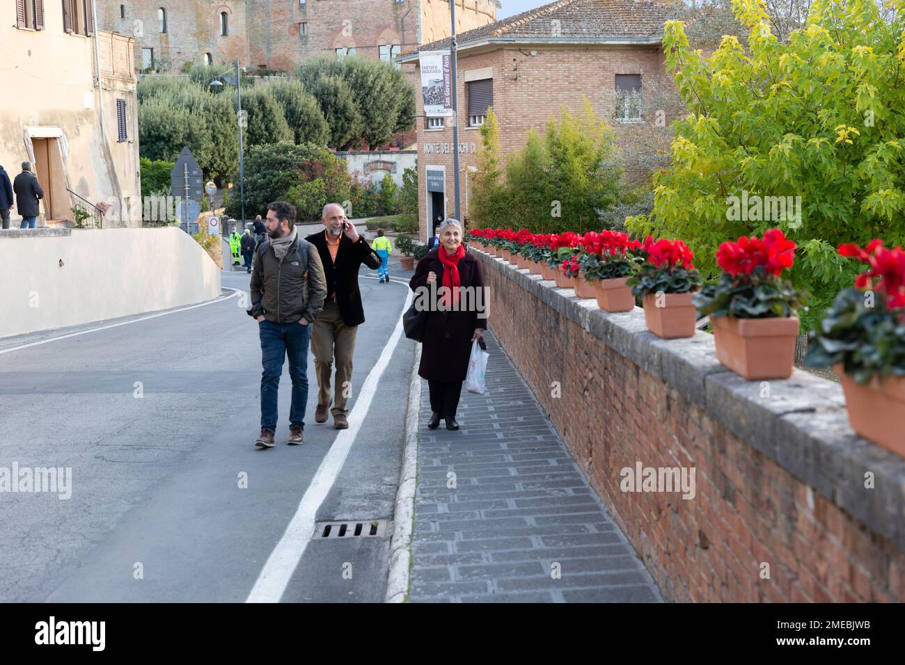 Three people walking down the road in the Tuscan village of San ...