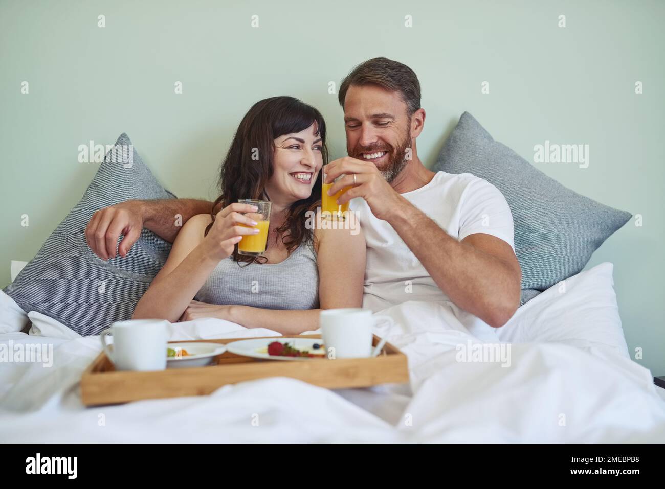 Cheers my dear. a cheerful young couple sitting in bed while enjoying ...