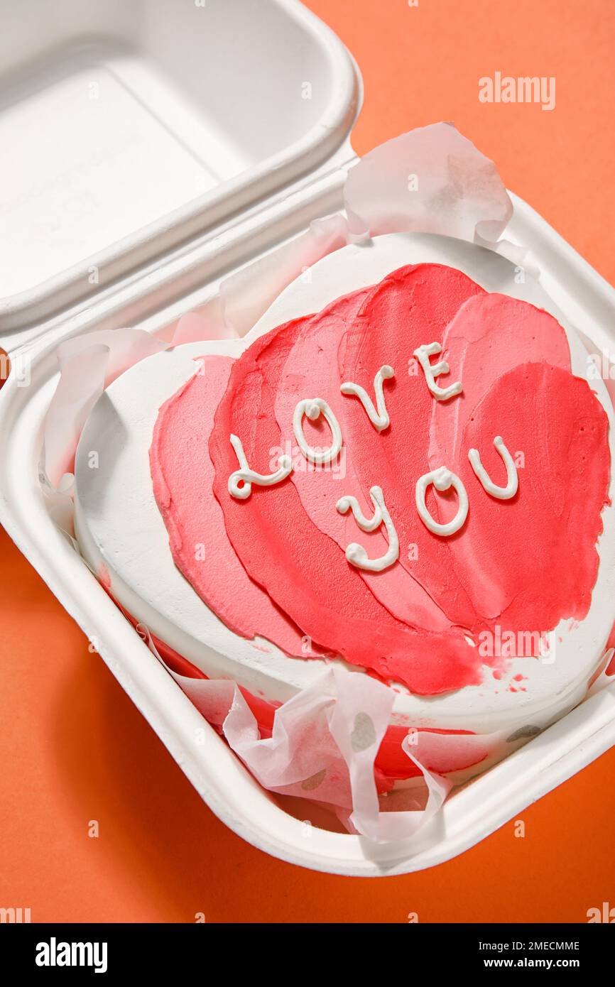 Plastic lunch box with heart-shaped bento cake on orange background ...