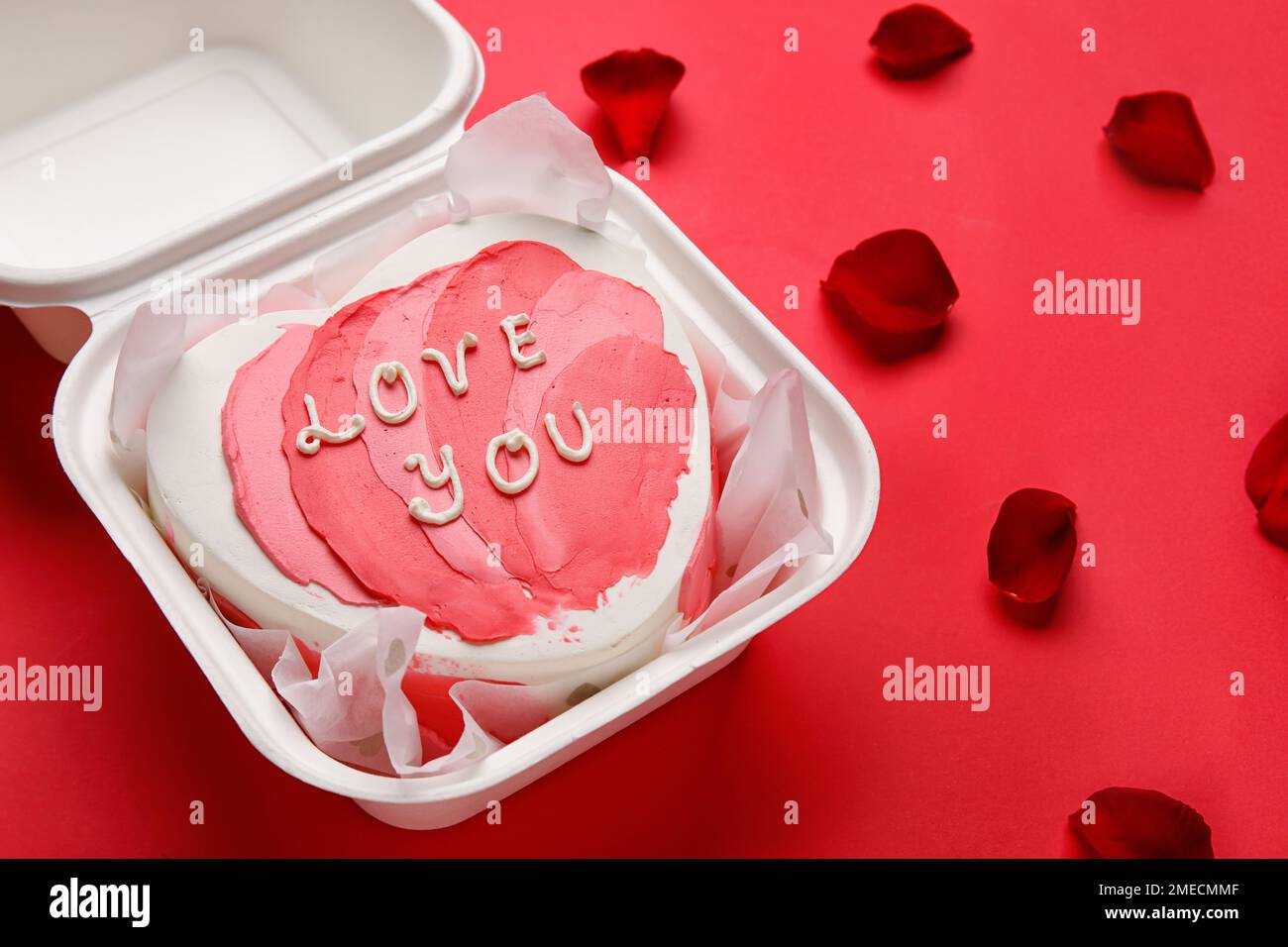 Plastic lunch box with heart-shaped bento cake and rose petals on red ...