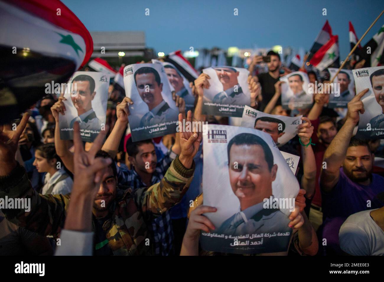 Syrian President Bashar Assad supporters hold up national flags and ...