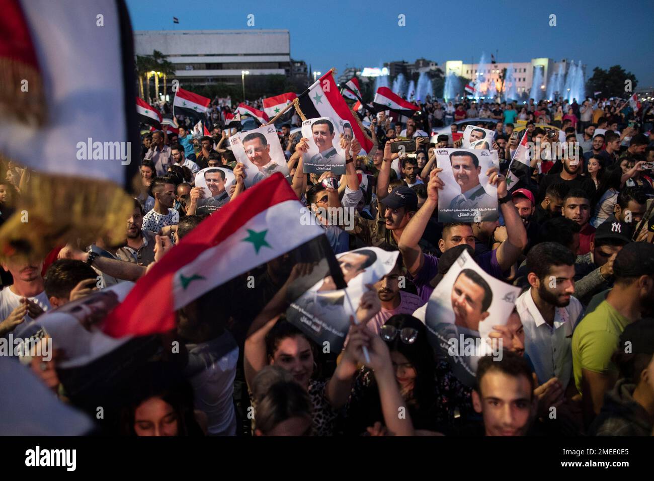 Syrian President Bashar Assad supporters hold up national flags and ...