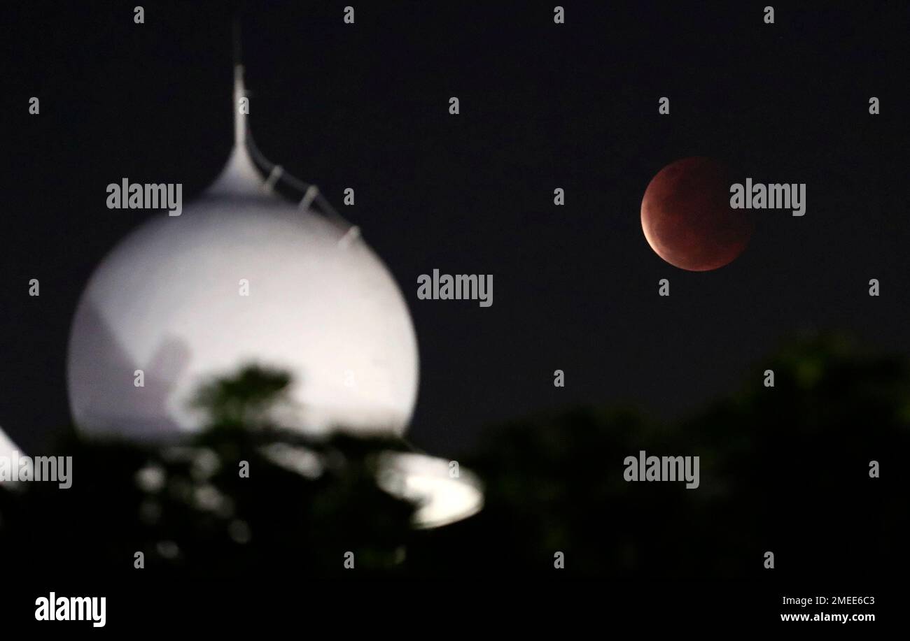 A full moon rises over a a mosque as a total lunar eclipse was taking ...