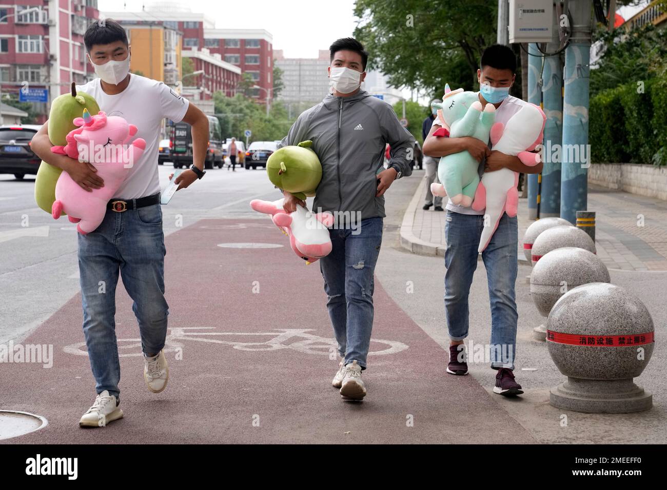 Chinese men wearing masks and carrying soft toys walk on the street in ...