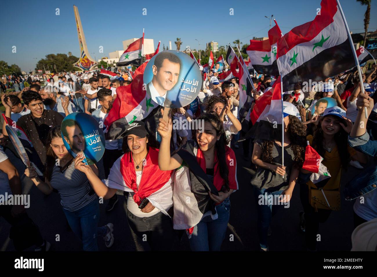 Syrian President Bashar Assad supporters hold up national flags and ...