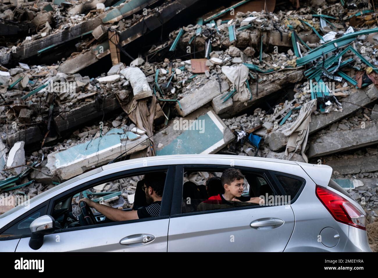 Cars full of spectators drive by the rubble of the al-Jalaa building ...