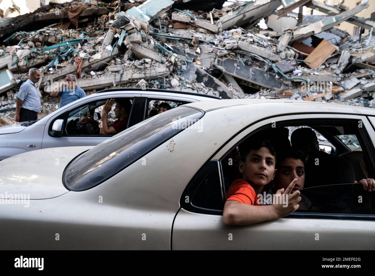 Cars full of spectators drive by the rubble of the al-Jalaa building ...