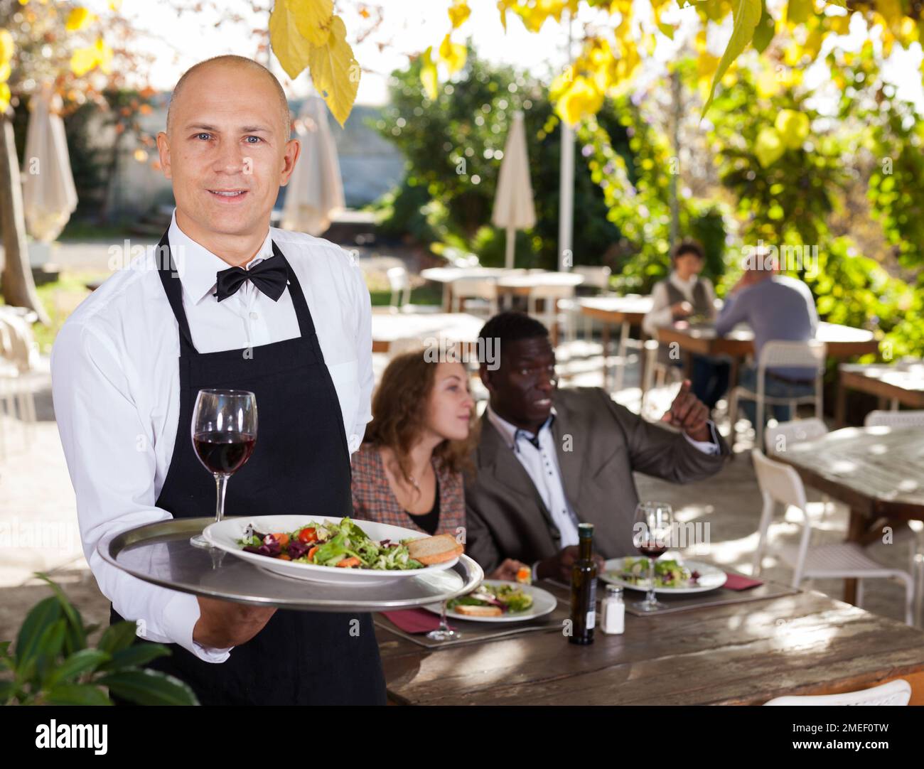 Adult waiter serves customers in a open-air restaurant Stock Photo - Alamy