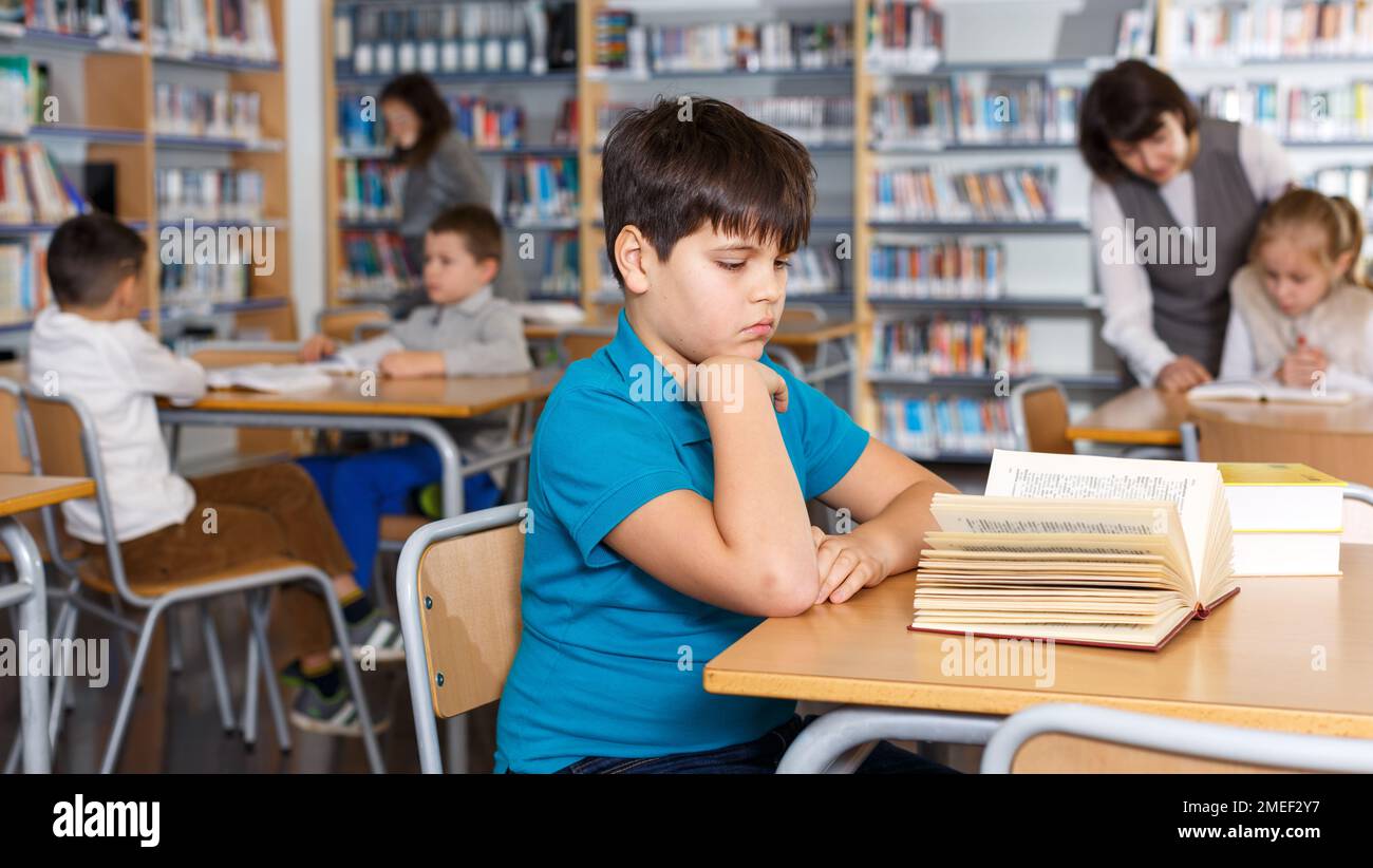 Tween boy reading textbooks in school library Stock Photo - Alamy