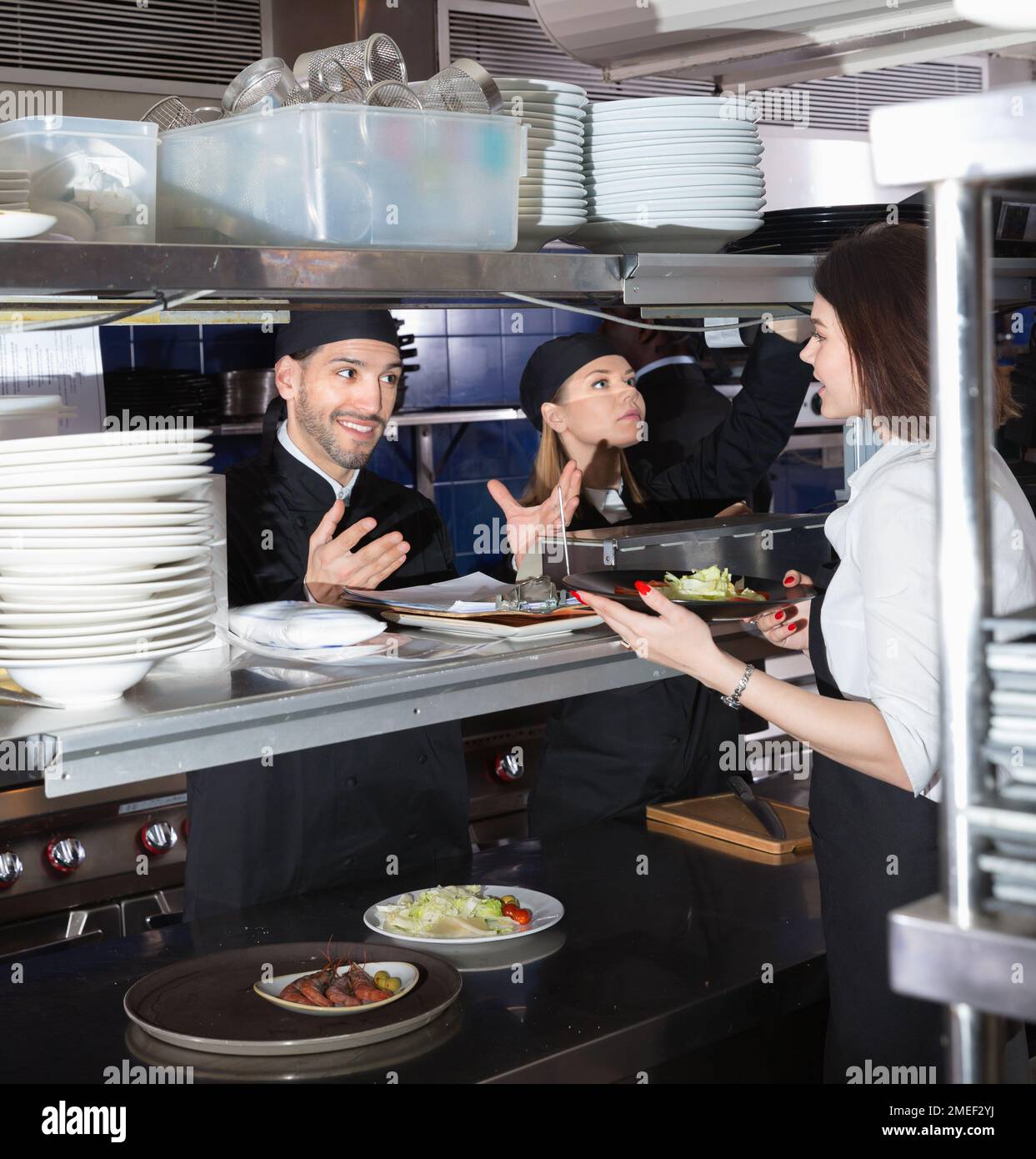 Woman waiter is giving order to chef cook on kitchen in restaurant ...