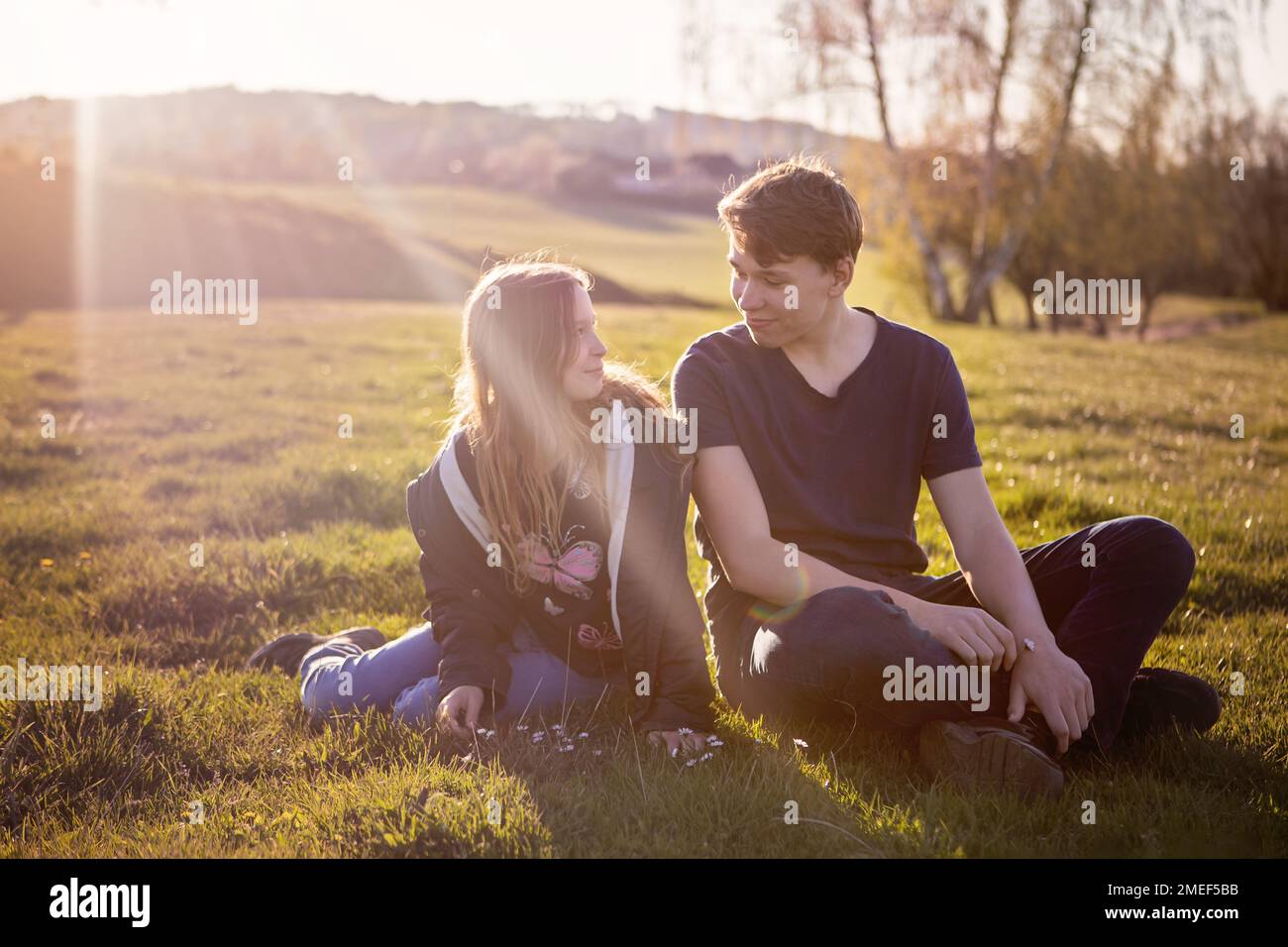 Brother and sister, siblings, boy and girl, sitting next to each other ...