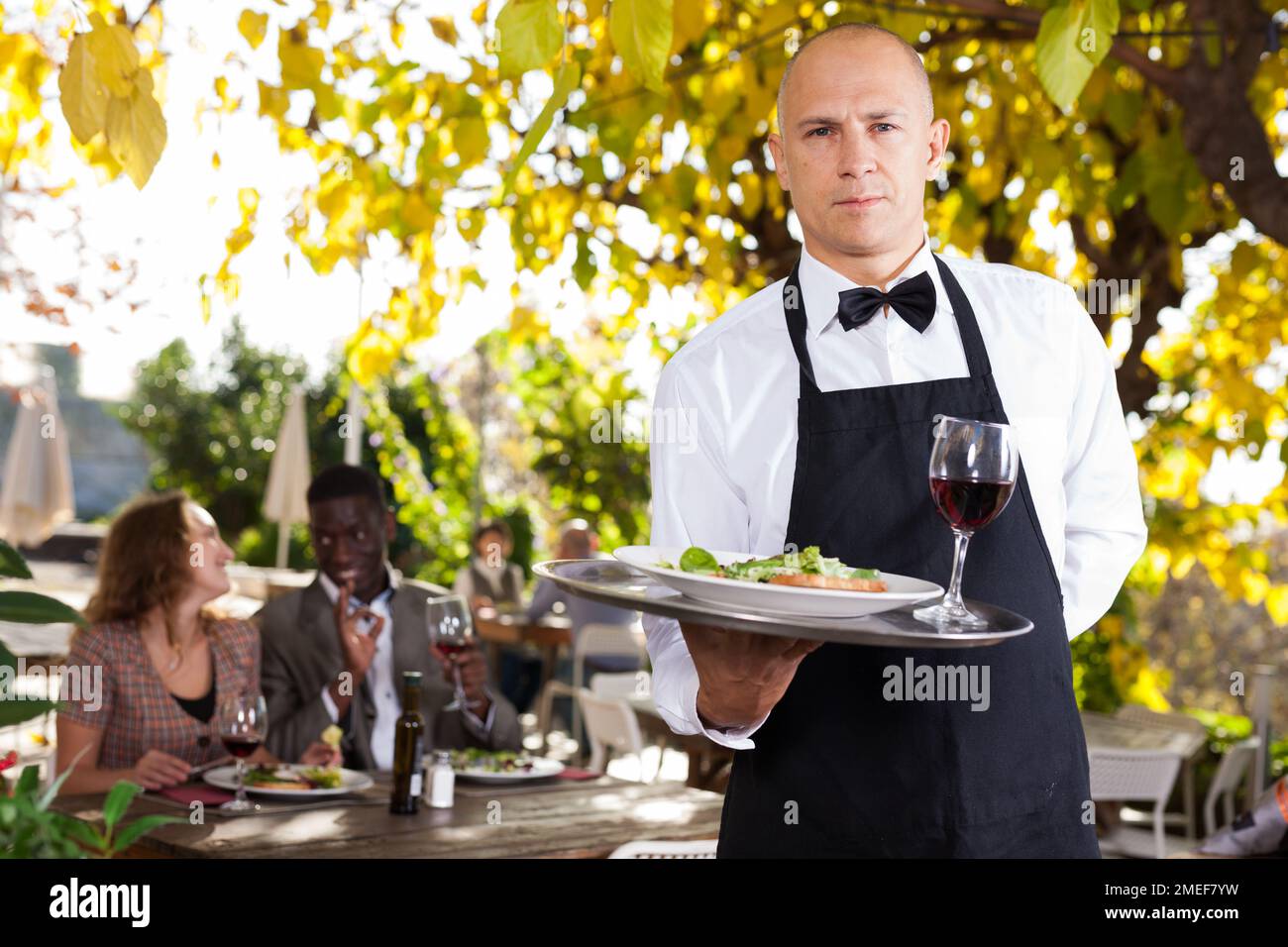 Adult waiter serves customers in a open-air restaurant Stock Photo - Alamy