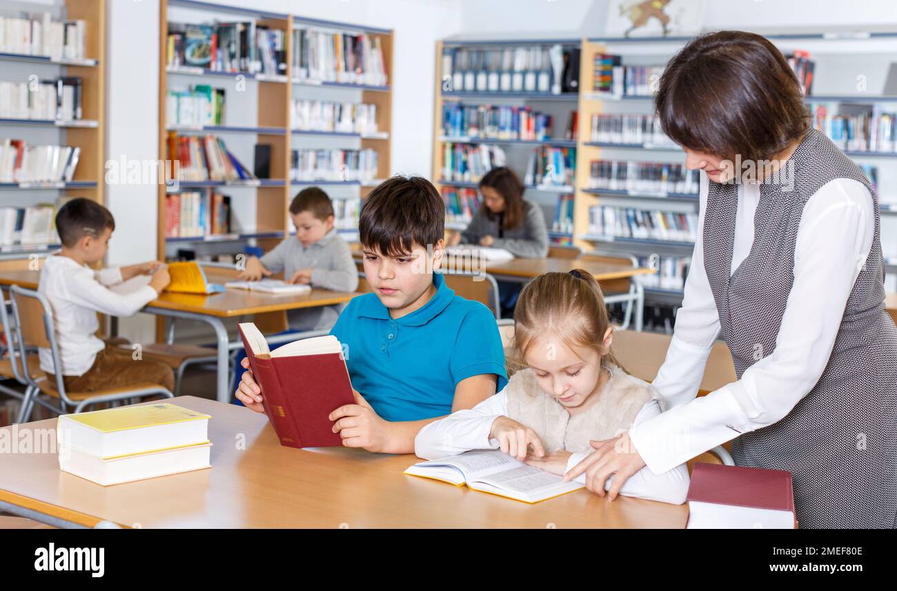Female librarian and schoolkids during classes in library Stock Photo ...