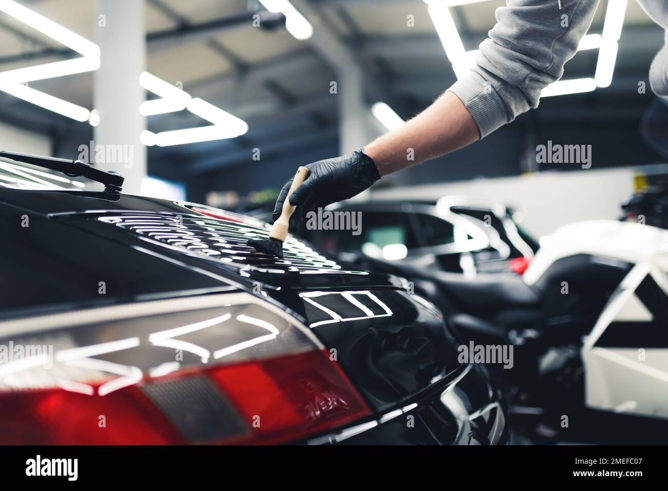 Close-up of male hand in black glove brushing trunk of black car ...