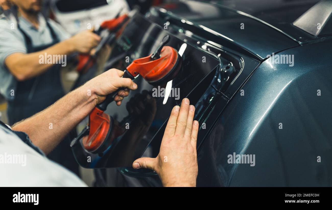 Close-up of two unrecognisable men holding rear window pane to install ...