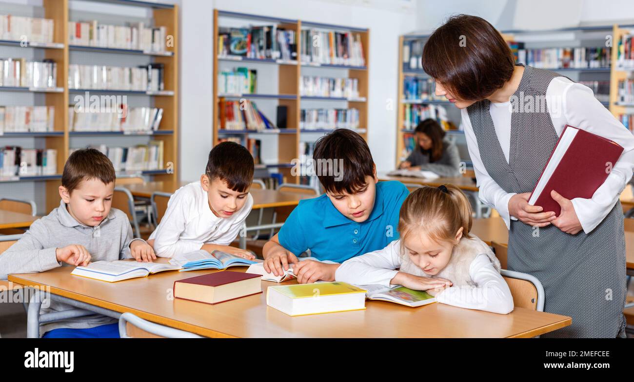 Group of school kids studying in school library with friendly female ...