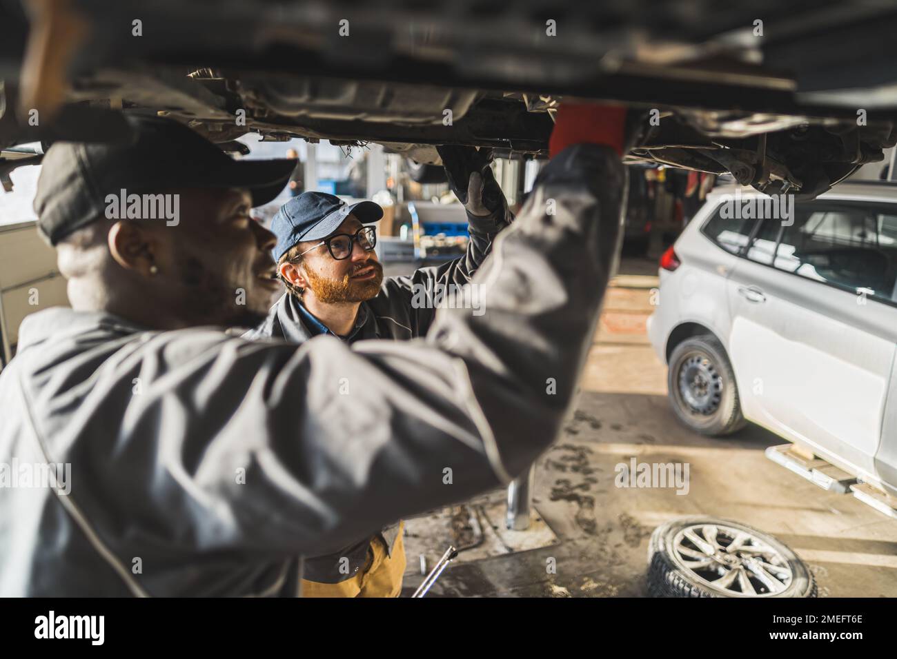 Close shot of two mechanics looking at a car's chassis while doing a ...