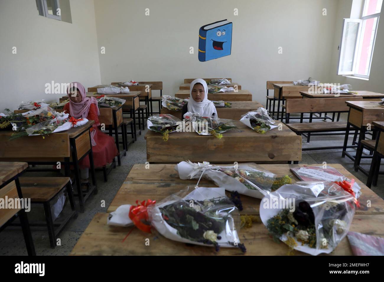 Schoolgirls sit inside a classroom with bouquets of flowers on empty ...