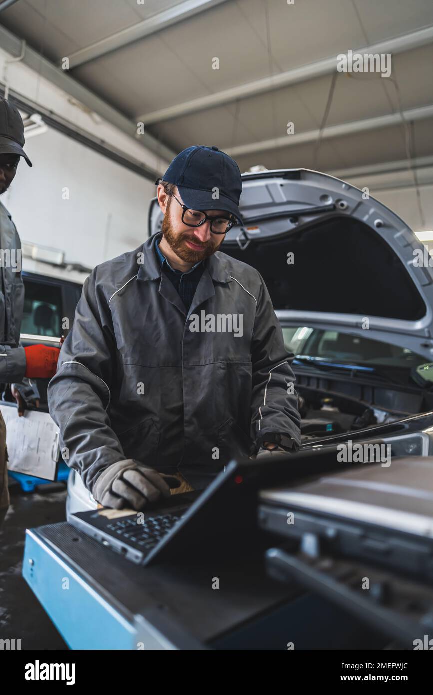 Vertical photo. Medium shot. A white male mechanic doing a computer diagnostics in a repair shop ...