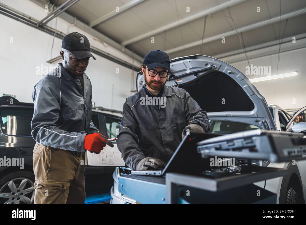 Medium shot of two mechanics doing computer diagnostics of a car and ...