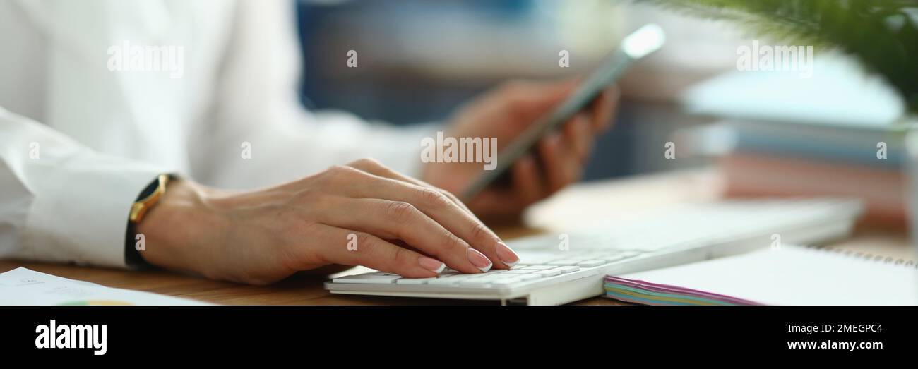 Female hands hold smartphone and work on laptop keyboard Stock Photo ...