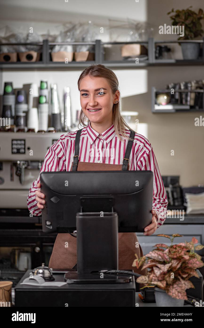Young barista girl near a cash-register. Young barmaid using modern ...
