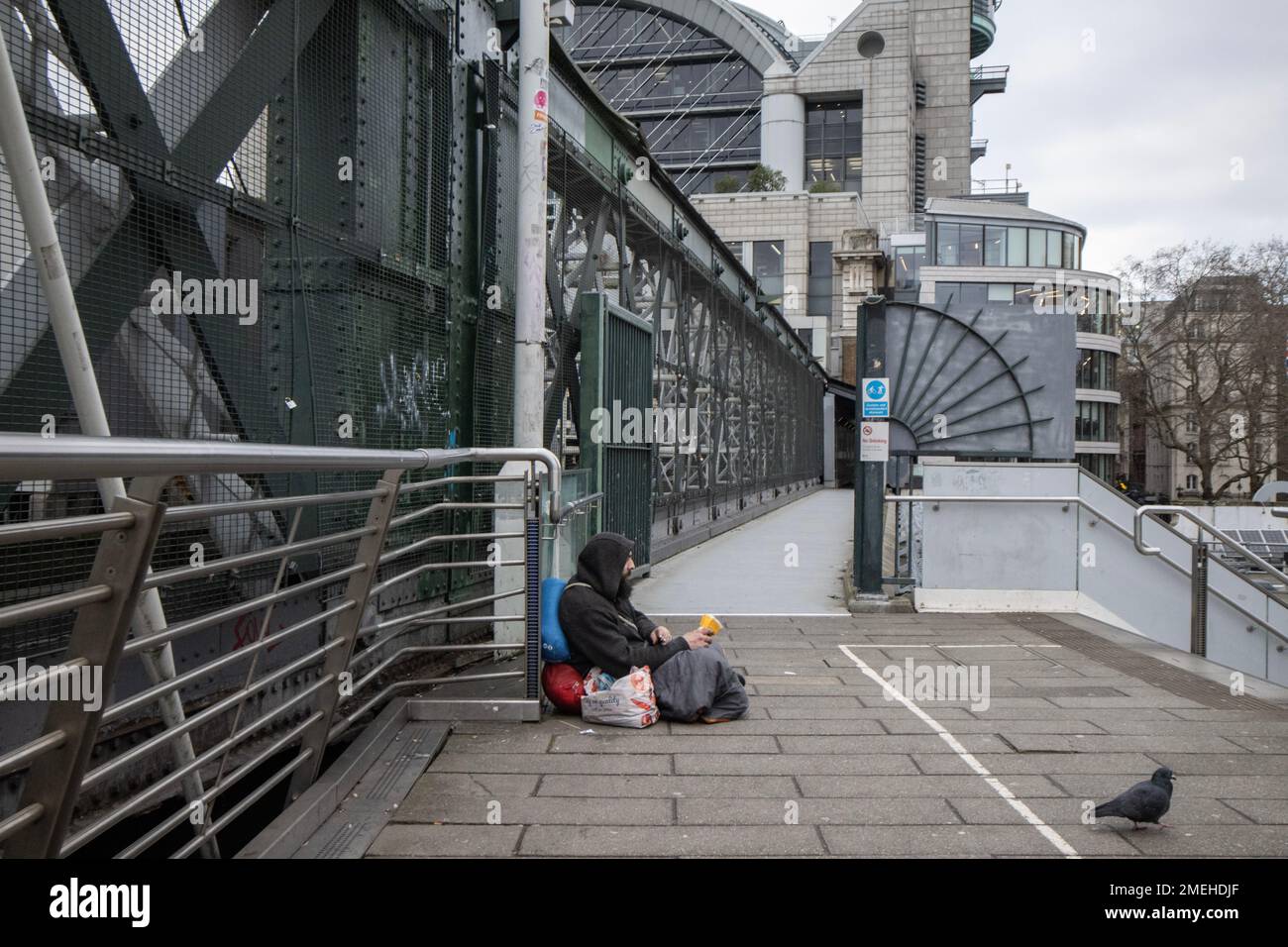 Homeless man sits on the concrete Hungerford footbridge at the entrance ...