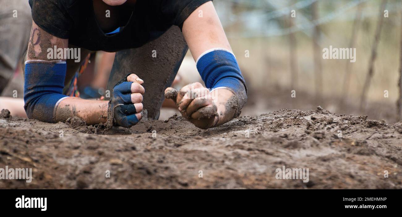 Mud race runners. Crawling,passing under a barbed wire obstacles during ...