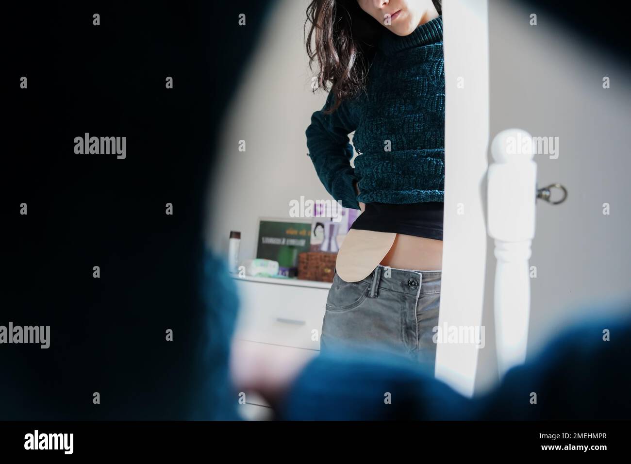 A female colon cancer survivor looking at the ostomy bag in the mirror ...