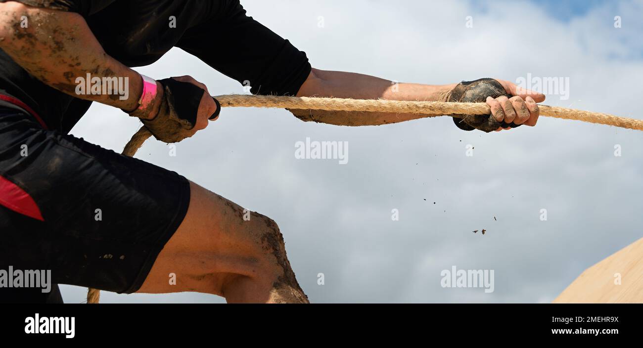 Mud race runners, defeating obstacles by using ropes Stock Photo - Alamy