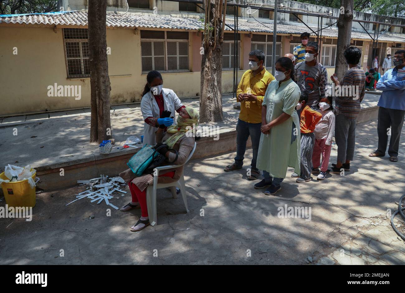 A health worker takes a nasal swab sample of a woman as others wait to ...