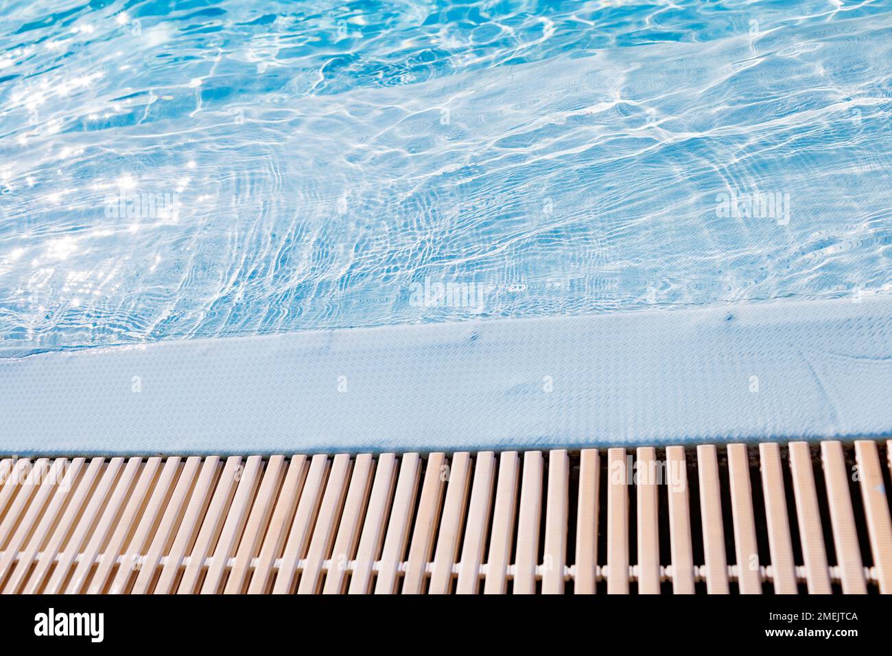 The edge of a shallow pool with clear, shiny, calm water and a wooden ...