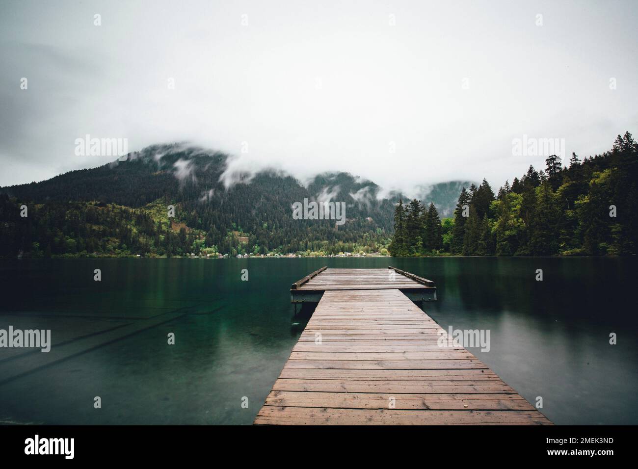 A wooden dock on a lake and a mountain of evergreen trees covered with ...