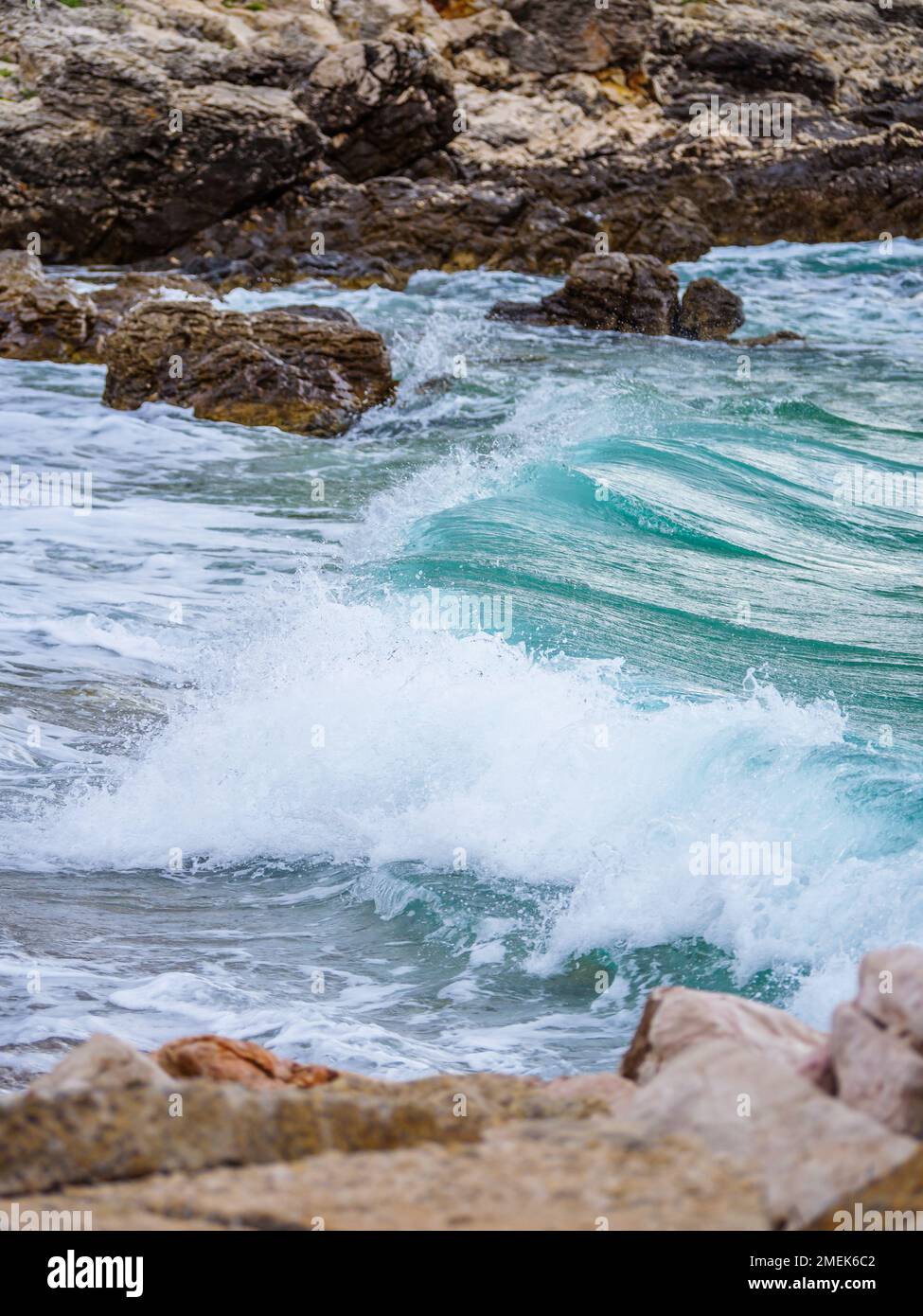 A vertical of a water splash, foamy turquoise sea waves splashing onto ...