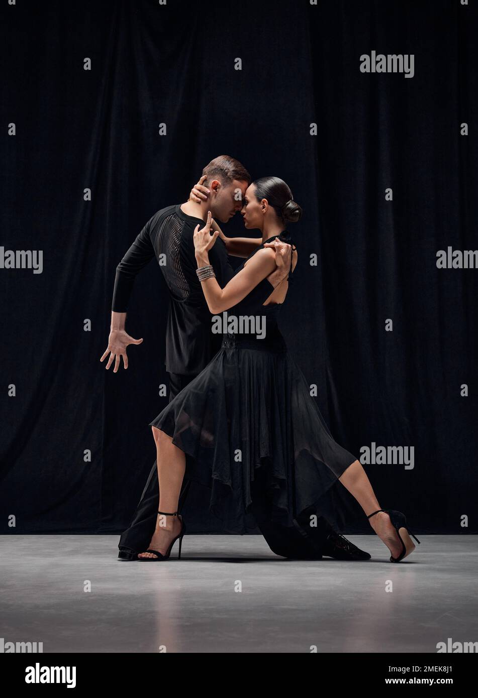 Man and woman, professional tango dancers performing in black stage costumes over black ...