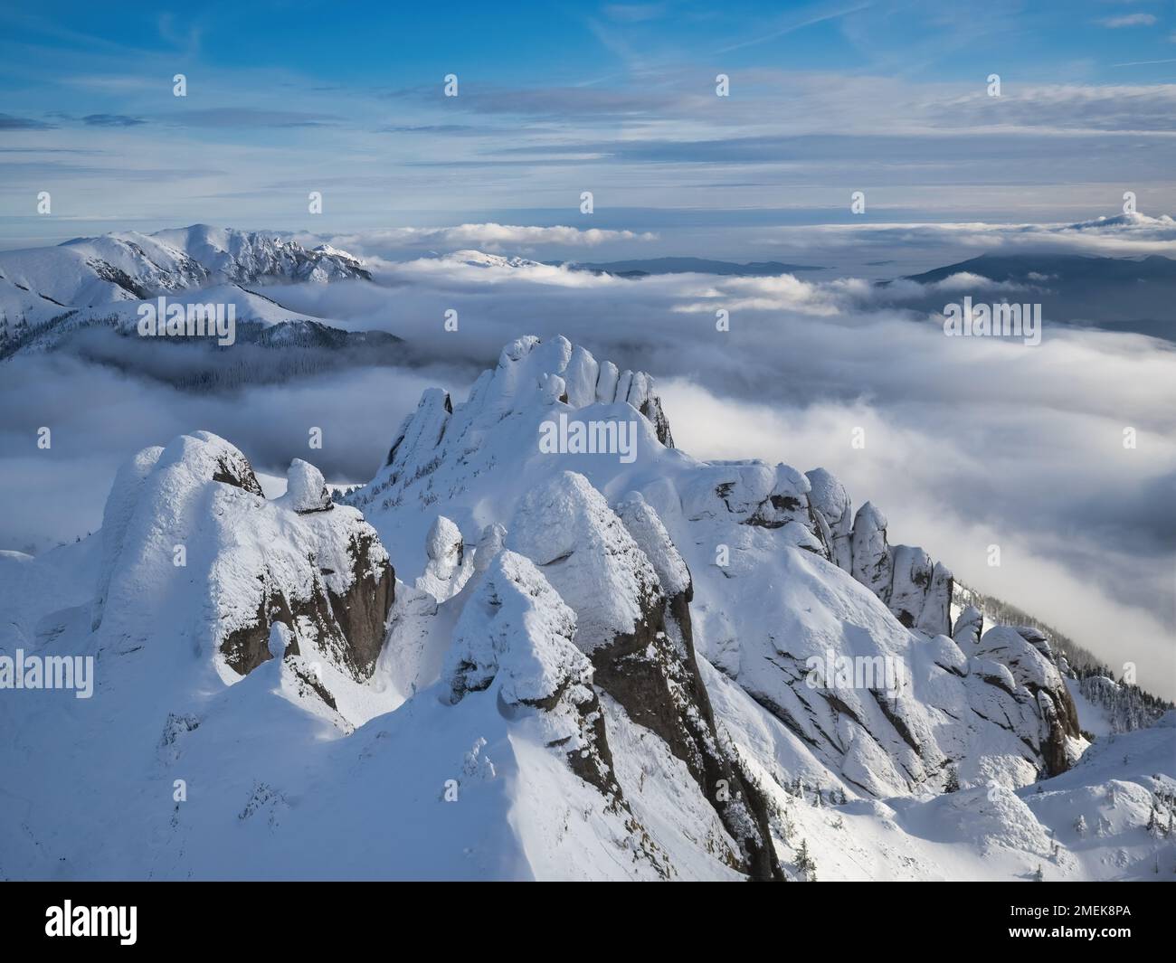 Aerial view of distant mountain peaks above clouds in clear sunny blue ...