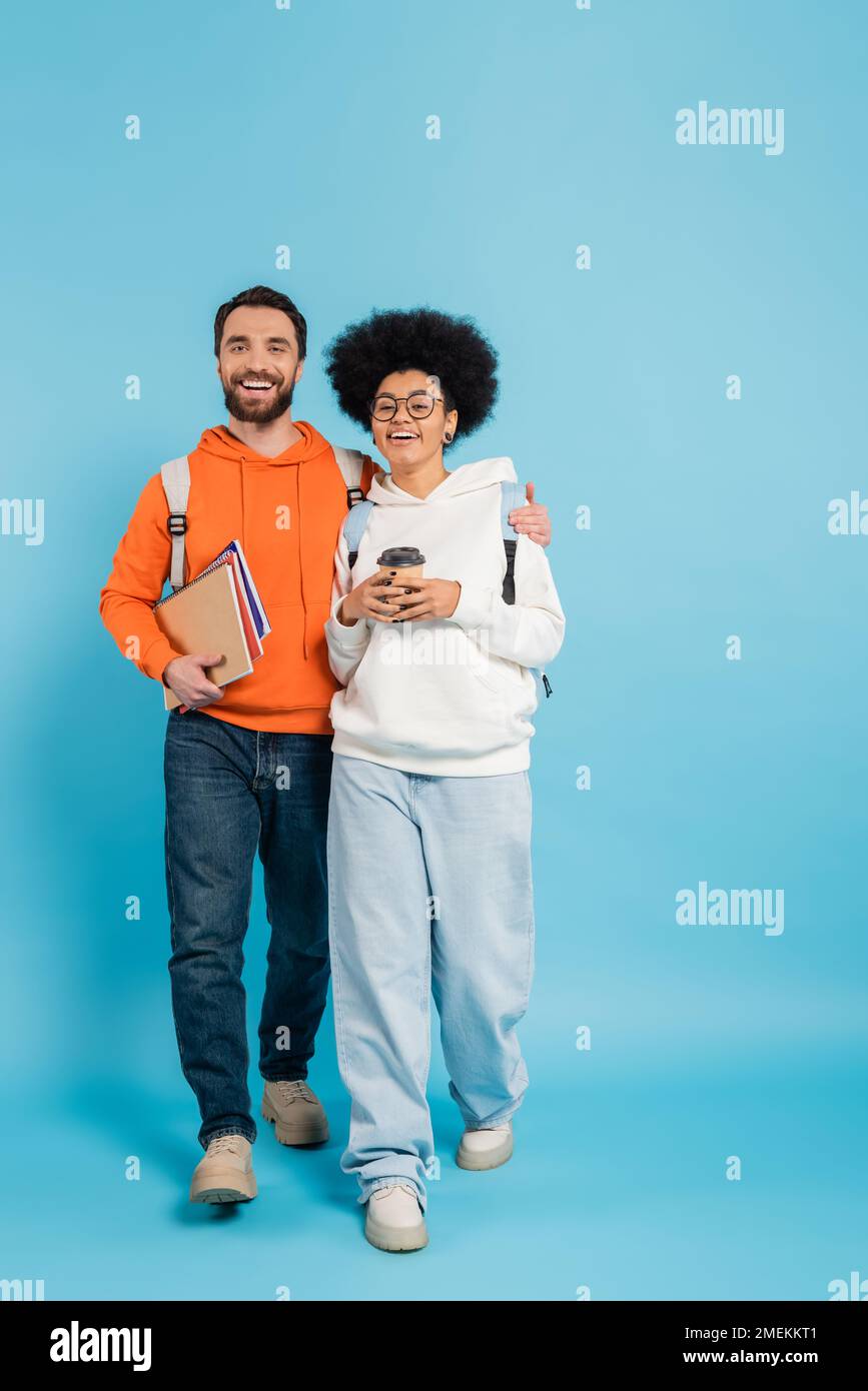 bearded student with notebooks hugging african american girlfriend with ...