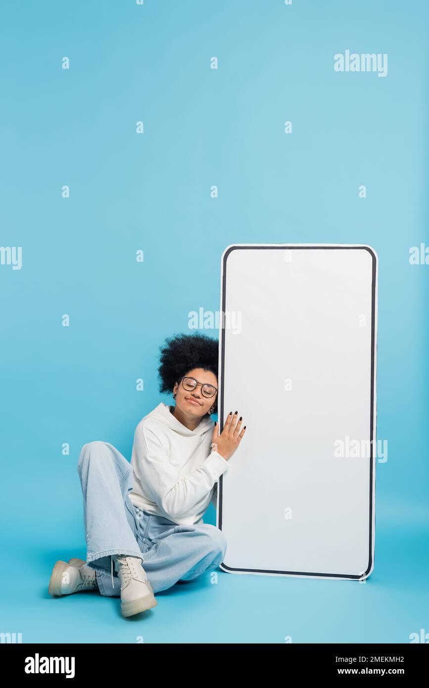 curly african american woman in eyeglasses and hoodie leaning on phone ...