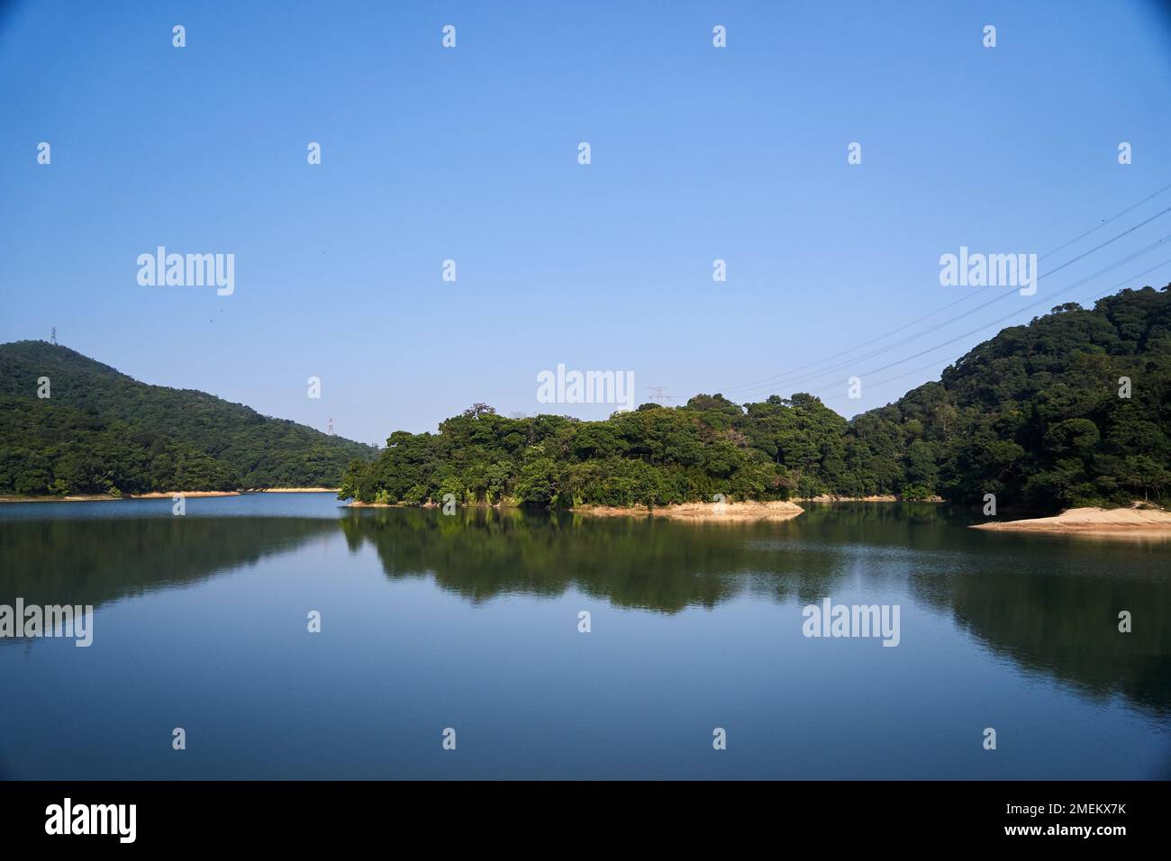 A landscape scene of trees reflecting on the lake with blue sky in ...