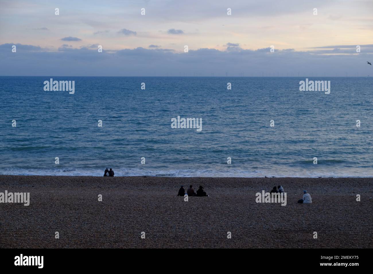 A sea view with people sitting on the sand of the beach at sunset time ...