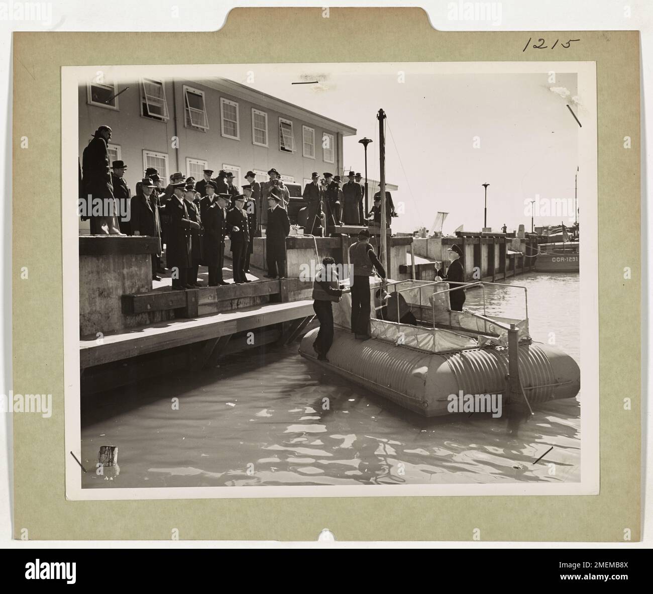 A group of Coast Guardsmen stand on a dock, observing a small craft ...