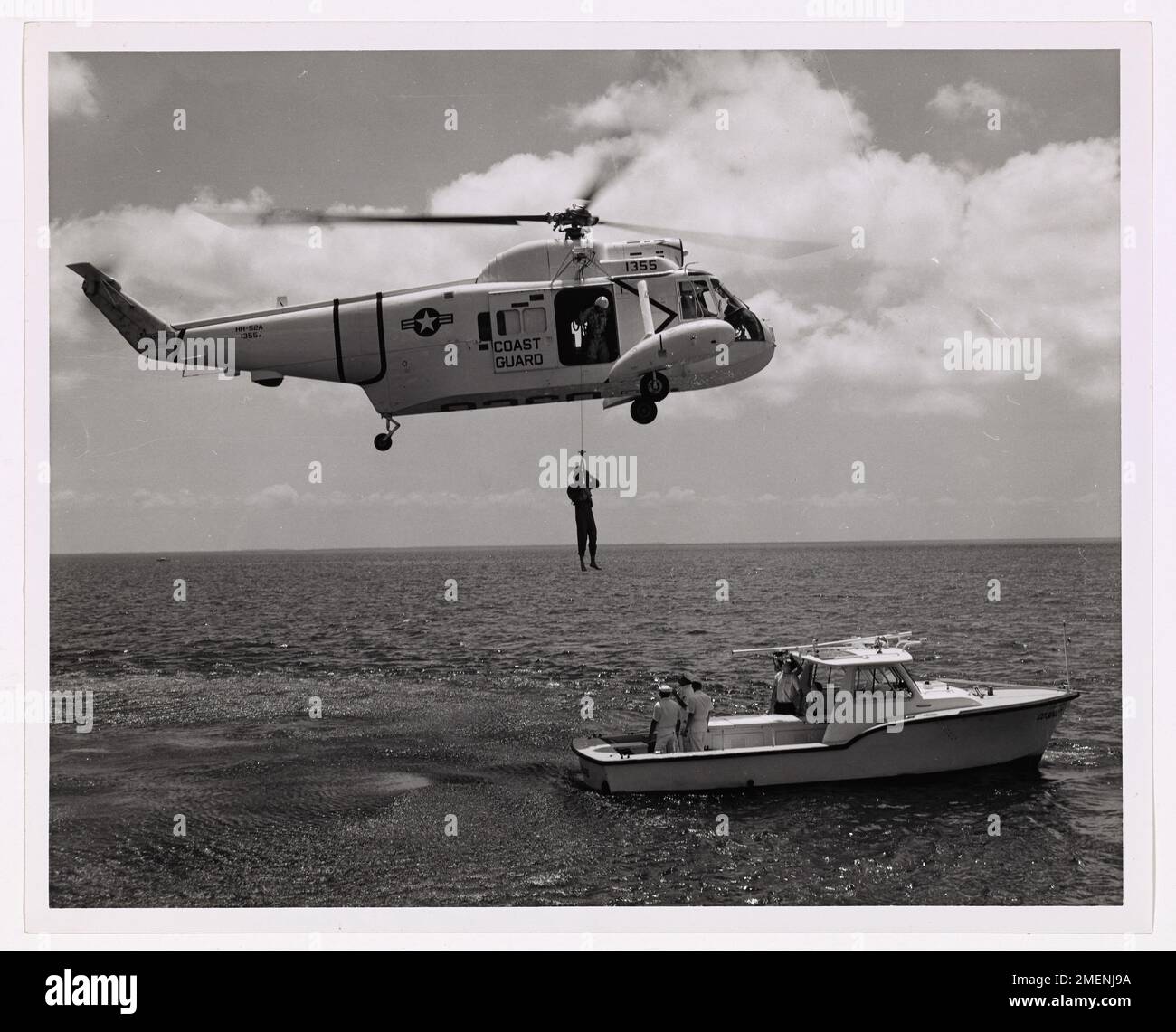 This image shows a Coast Guard helicopter performing a hoist ...