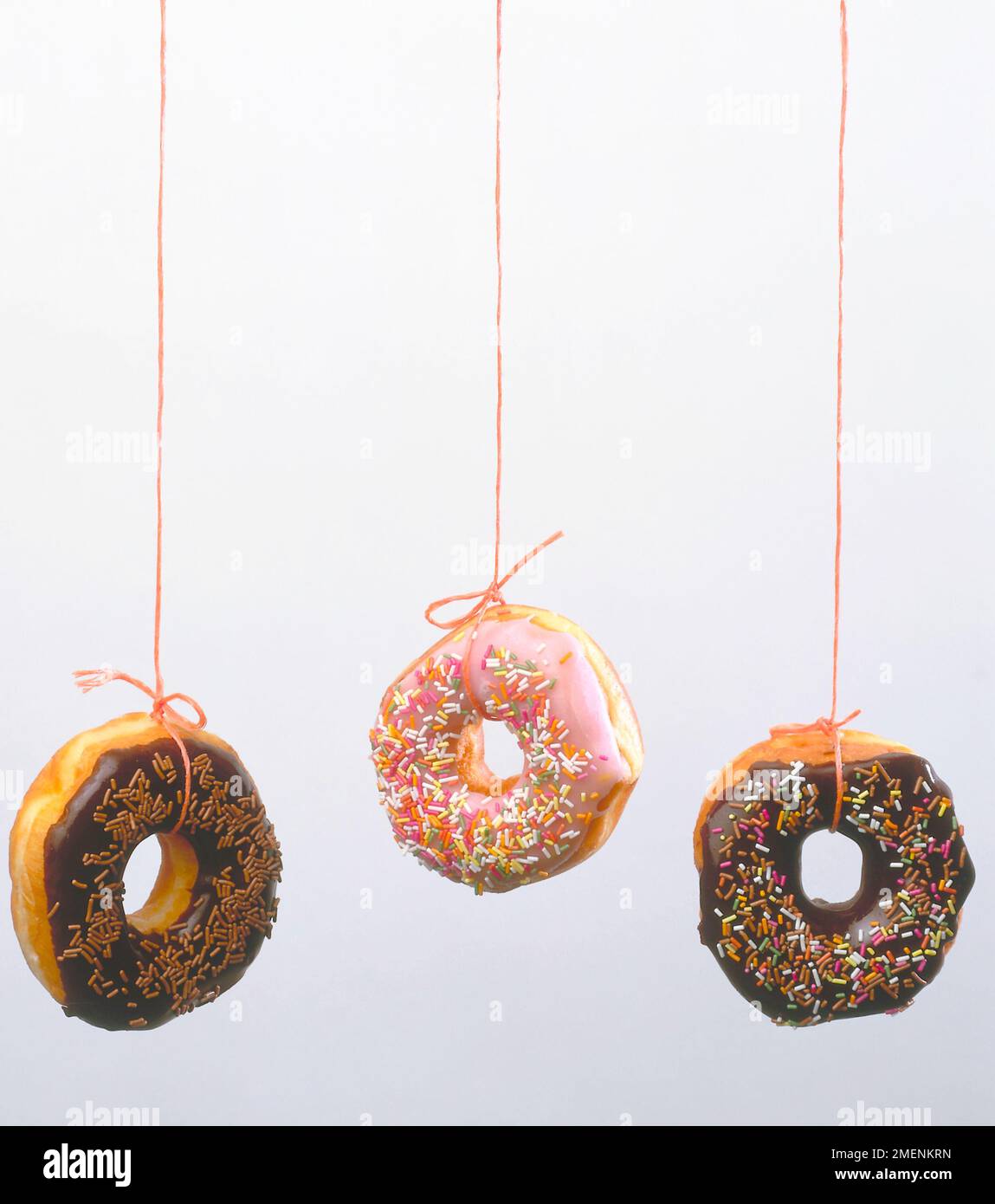 Iced doughnuts covered in hundreds and thousands, hanging on string Stock Photo - Alamy